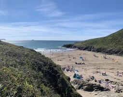 Uma praia com pessoas tomando sol e nadando, cercada por falésias rochosas e vegetação.