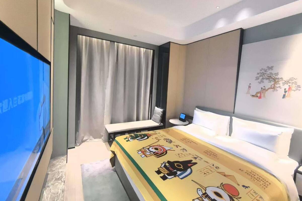 Quarto de hotel moderno com uma cama grande, televisão, escrivaninha e janela com cortinas.