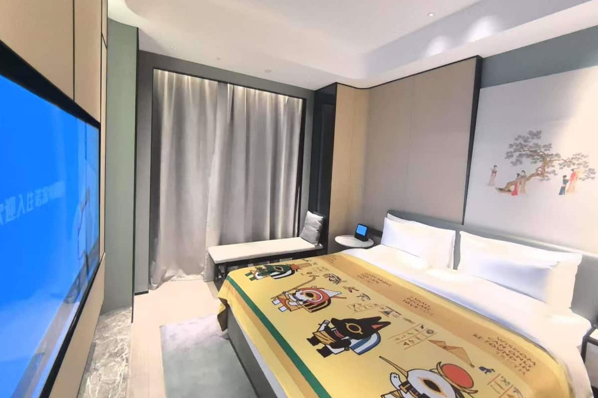 Quarto de hotel moderno com uma cama grande, televisão, escrivaninha e janela com cortinas.