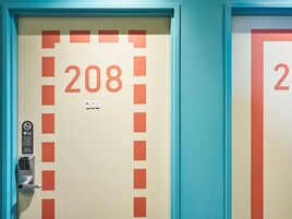 Porta de quarto de hotel com o número 208, fechadura eletrônica e placa indicando código de 6 dígitos e botões.