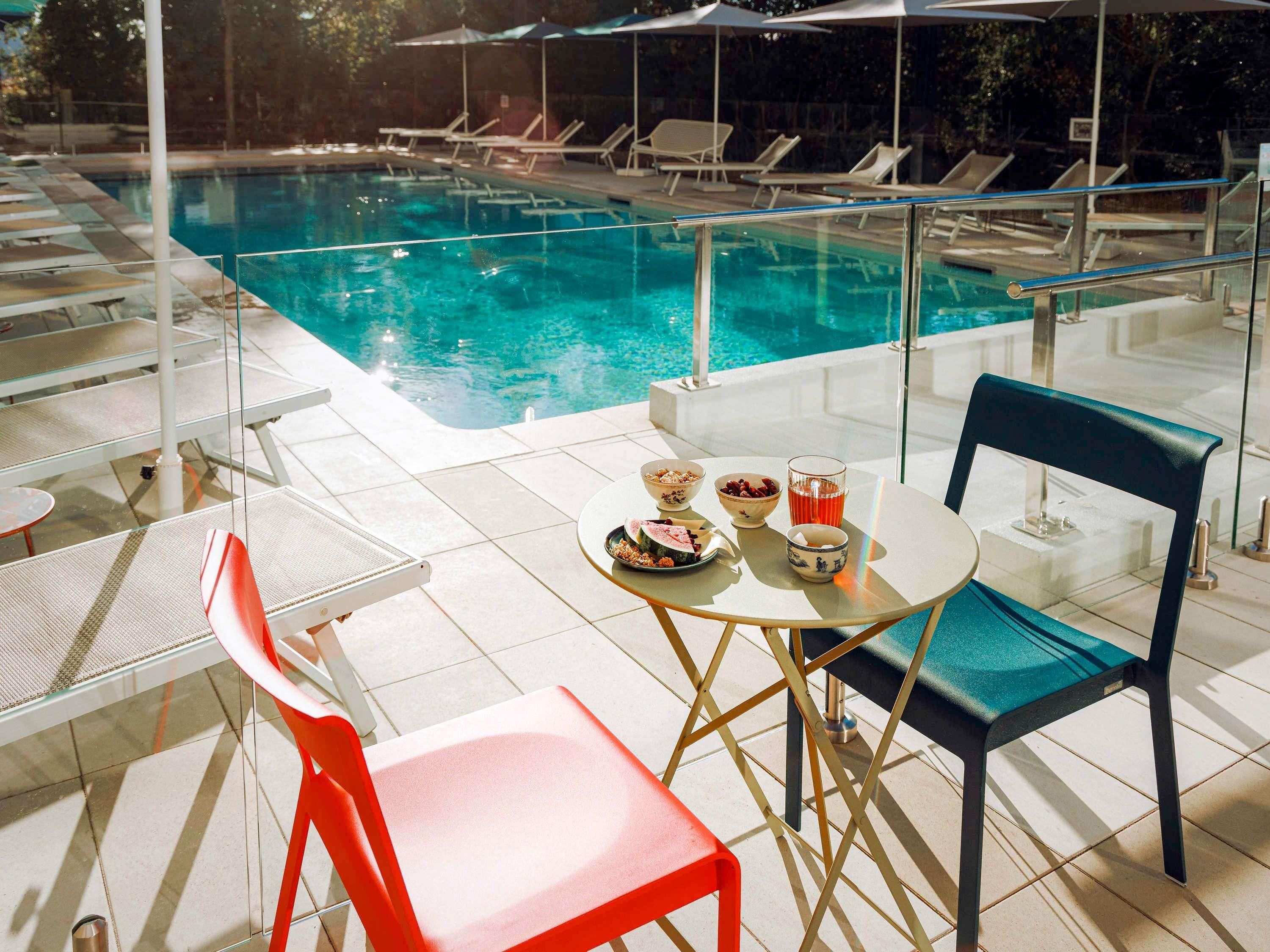 Área de piscina com mesa, cadeiras e guarda-corpo de vidro.