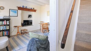 Uma sala de estar com estante, televisão de tela plana, lareira, área de jantar e escada.