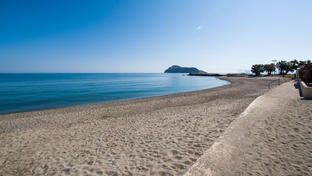 Uma praia com um calçadão de concreto, um pequeno edifício e uma ilha ao longe.