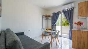 Uma sala de estar moderna com um sofá cinzento, uma mesa de jantar com cadeiras e uma área de cozinha com uma pia e um vaso de flores.