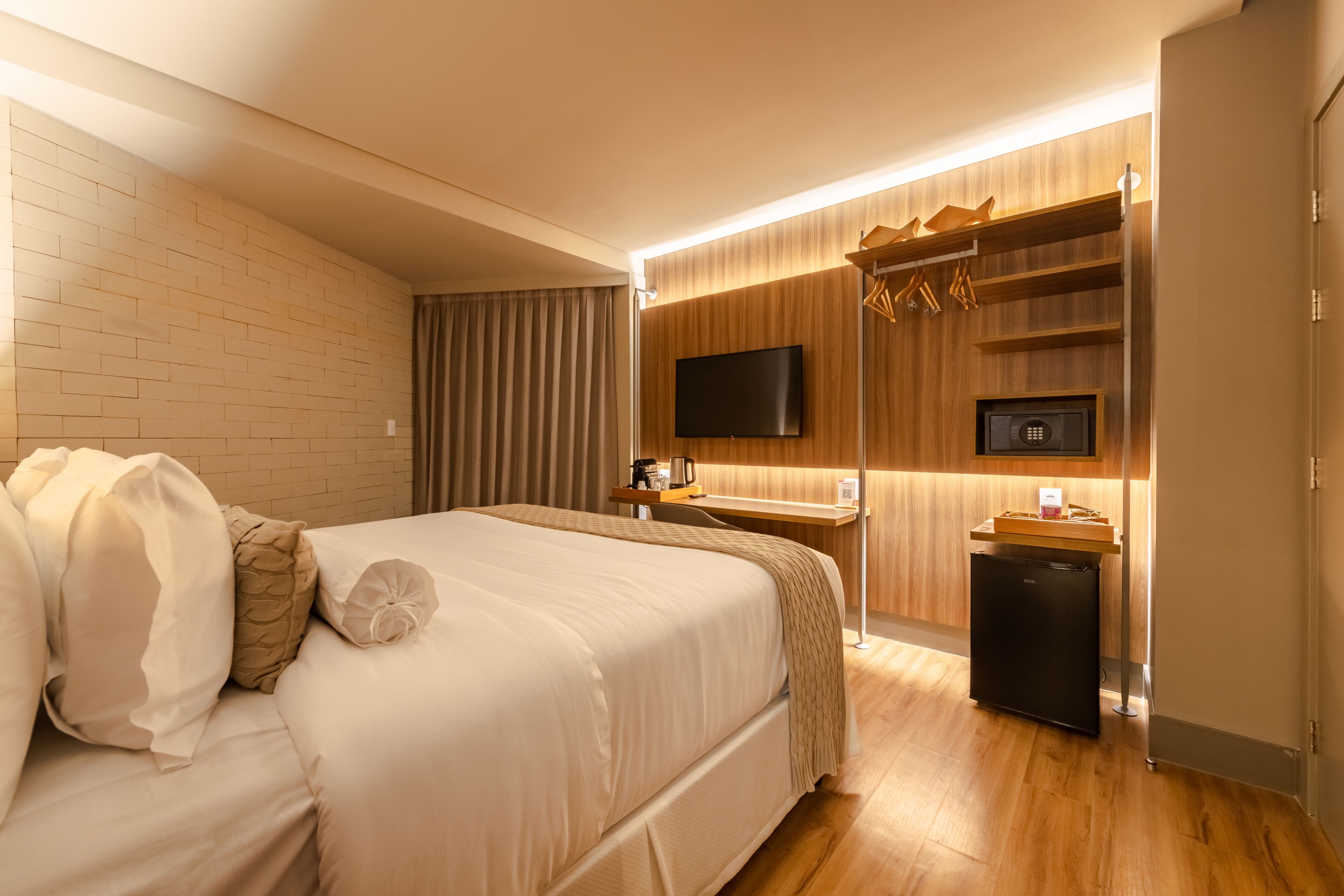Quarto de hotel com cama, escrivaninha, televisão e minibar.