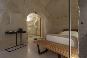 Quarto moderno com cama, um banco de madeira, uma mesinha e chuveiro de vidro.