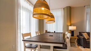 Uma sala de jantar com uma mesa de madeira, cadeiras brancas e luminárias pendentes de vime.