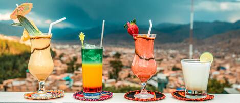 Quatro cocktails numa varanda com vista para a paisagem urbana.