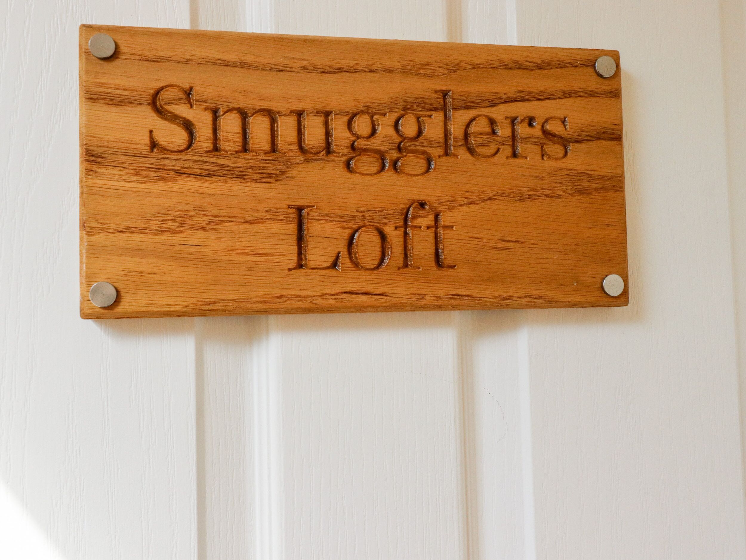 Uma placa de madeira com o texto 'Smugglers Loft' fixada em uma parede branca.