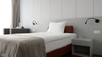 Quarto de hotel moderno com cama, mesa de cabeceira, cadeira e painel de cabeceira fixado na parede.