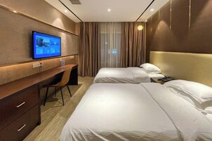 Quarto de hotel com cama, escrivaninha com computador, televisão e janela com cortinas.