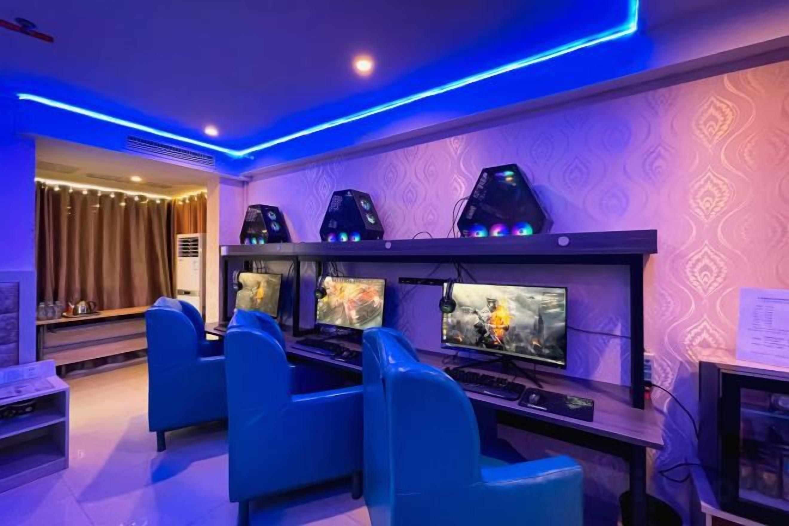 Sala de jogos com vários monitores, cadeiras gamer e iluminação em LED.