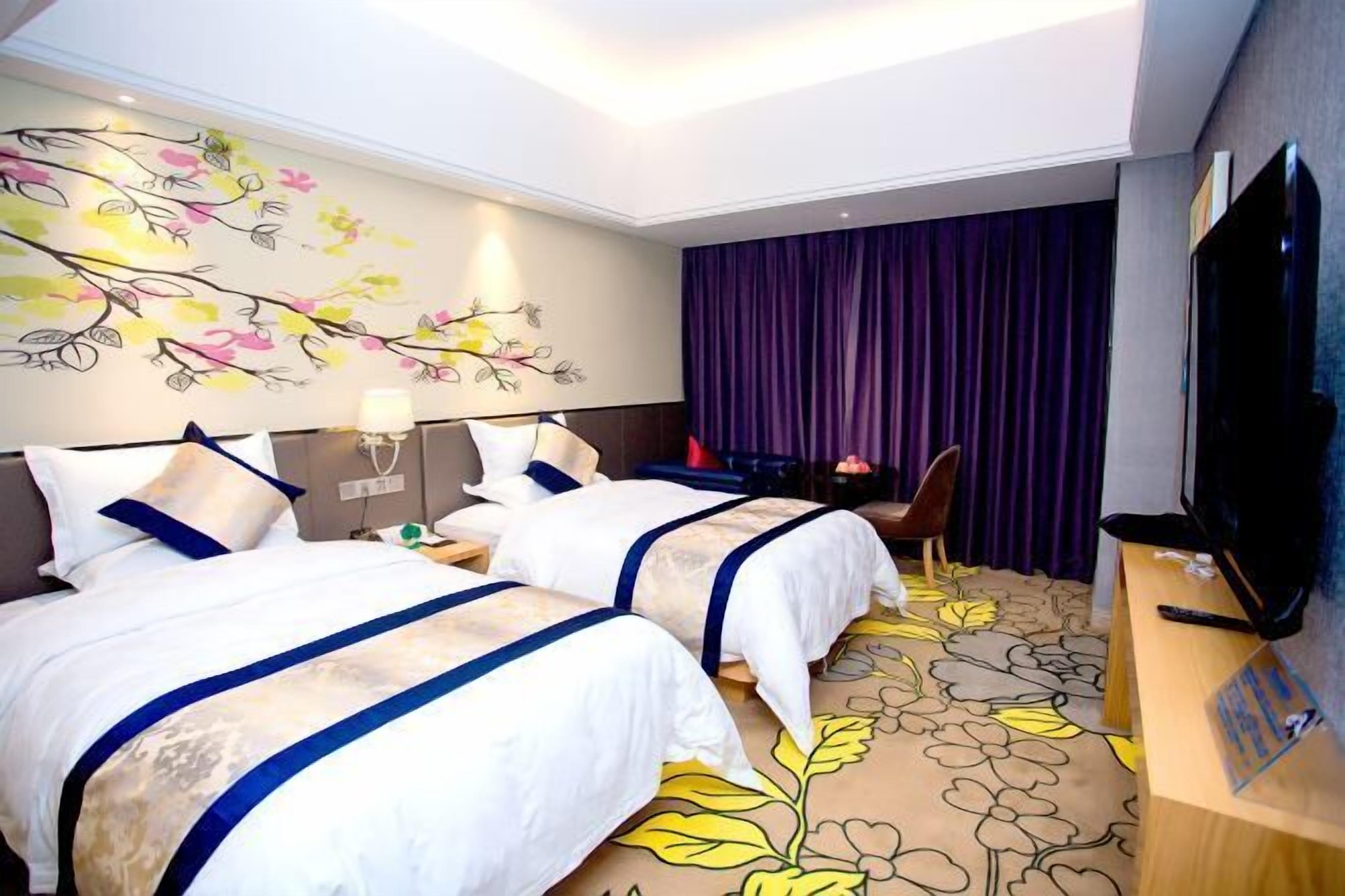 Quarto de hotel com duas camas, uma televisão, uma secretária e um mural floral na parede.