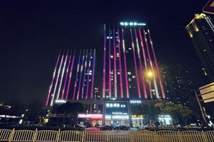 Um hotel com fachada moderna, linhas verticais iluminadas e uma placa visível com o nome.