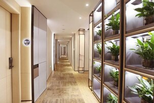 Um corredor de hotel com piso carpete, uma placa com o número 891 e prateleiras com plantas em vasos.
