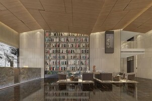 Um lobby moderno com uma recepção de mármore, uma grande estante de livros e uma área de estar com sofás e mesas.