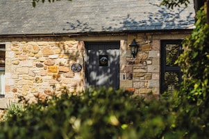 Uma casa de pedra com porta escura, caixa de correio e pequena janela.