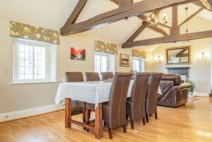 Uma sala de jantar com mesa posta para seis, vigas de madeira no teto e lareira com espelho acima.