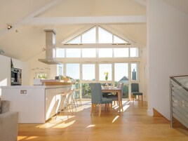Uma cozinha espaçosa com uma ilha grande, uma área de jantar com mesa e cadeiras, e vista para o exterior por grandes janelas.