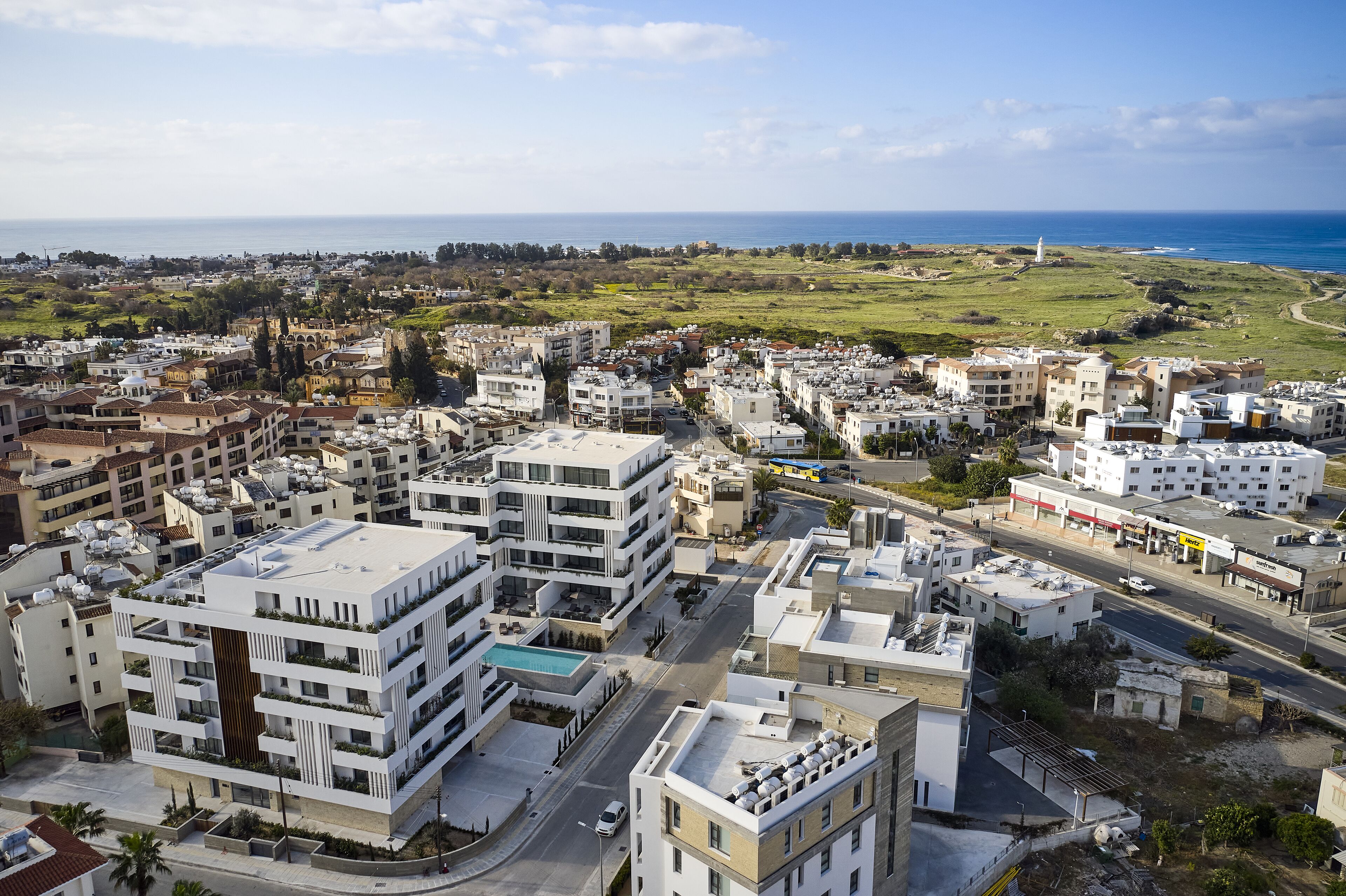 Paisagem costeira com edifícios modernos, vista clara do mar e um farol ao longe.