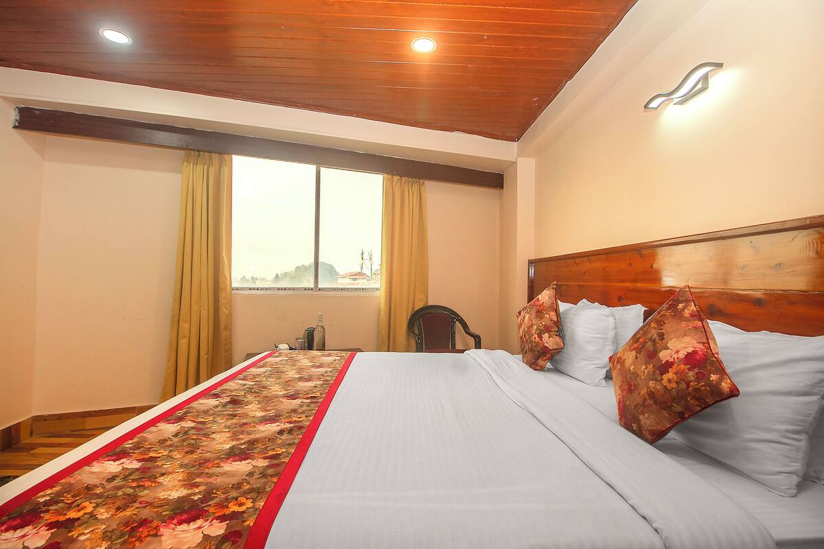 Quarto de hotel com teto de madeira, uma cama grande com roupa de cama floral, cabeceira de madeira e uma janela com cortinas.