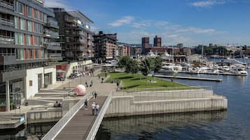 Um calçadão à beira-mar com edifícios modernos, um porto de iates e uma ponte para pedestres.