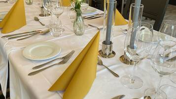 Mesa posta para um jantar formal, com toalha branca, guardanapos dourados e copos de vidro transparente.