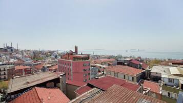 Paisagem urbana com um edifício de telhado vermelho em destaque no primeiro plano e vista para o mar ao fundo.