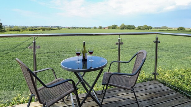 Um terraço com uma mesa e duas cadeiras, com vista para um campo verde.