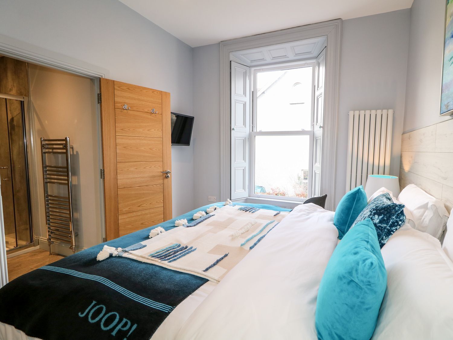 Quarto com cama, guarda-roupa de madeira, radiador e janela com vista.