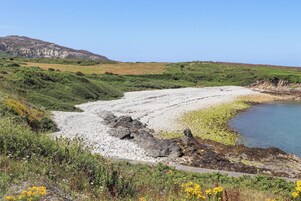 Paisagem costeira com linha de costa rochosa, vegetação verde e céu claro.