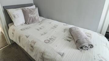 Uma cama de solteiro com colcha listrada e duas almofadas, uma delas com um bordado de nome.