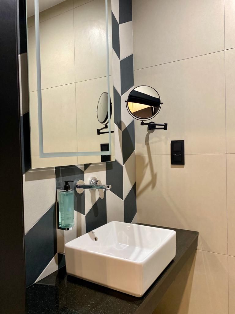 Um banheiro moderno com pia branca, paredes revestidas com azulejos preto e branco e um espelho grande.