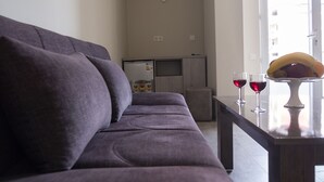 Uma sala de estar moderna com um sofá cinzento, uma mesinha com duas taças de vinho e uma fruteira.