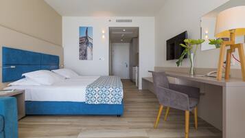 Quarto de hotel moderno com cama, escrivaninha, cadeira e televisão.