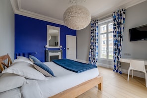 Um quarto com uma cama, cômoda, espelho, televisão e janela com cortinas.