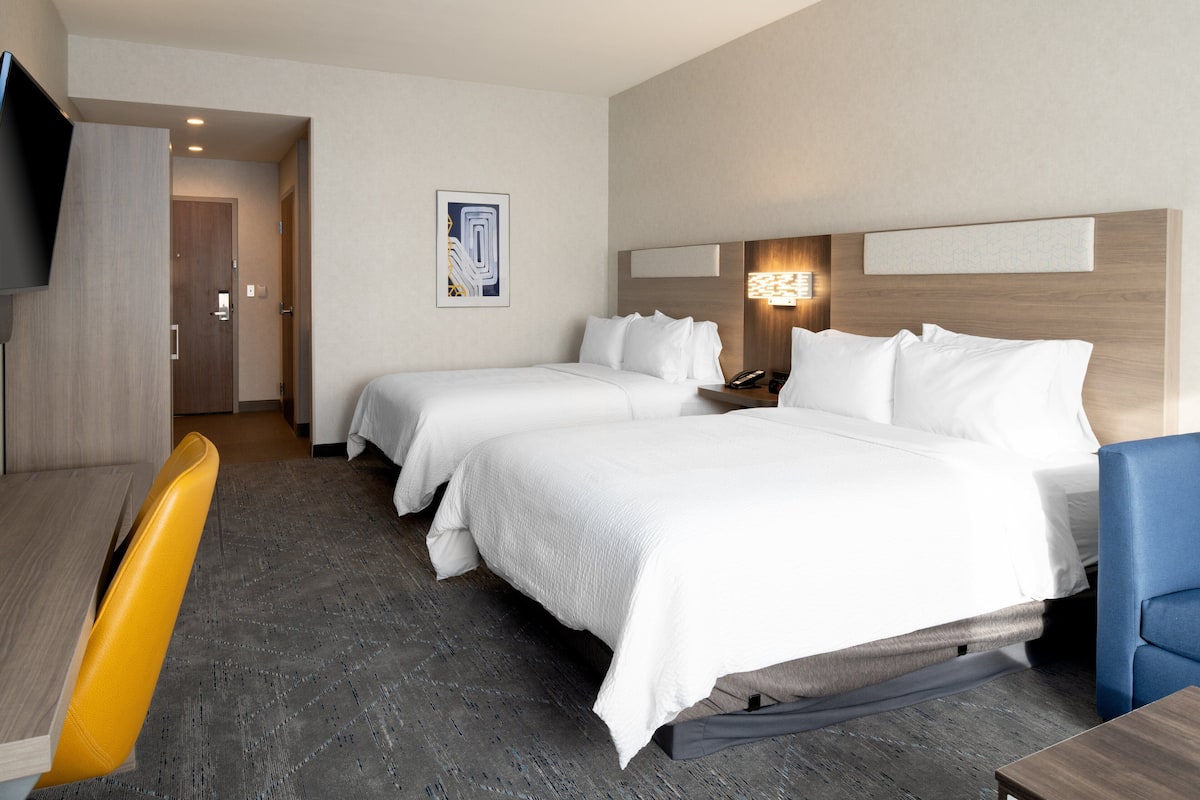 Quarto de hotel com duas camas, uma escrivaninha, uma cadeira e uma televisão.