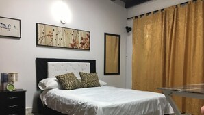Quarto com cama, mesa de cabeceira, luminária e uma parede decorada com obras de arte.