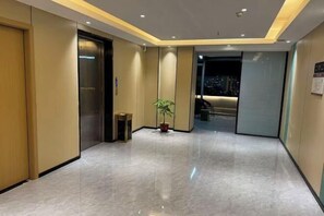 Um lobby de hotel moderno com piso de mármore, uma planta em vaso e um elevador.
