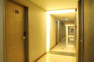 Corredor de hotel com portas, piso ladrilhado e teto com iluminação embutida.