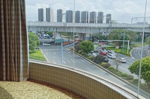 Vista da janela com uma rua movimentada, carros, uma ponte e edifícios altos ao fundo.