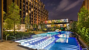Um hotel moderno com área de piscina no terraço, apresentando fontes iluminadas e vista para o horizonte da cidade à noite.