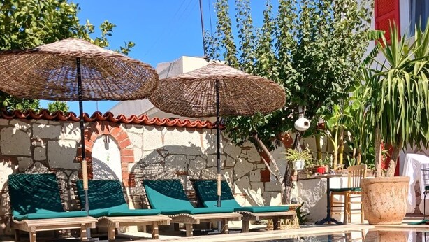 Piscina cristalina com espreguiçadeiras e guarda-sóis, cercada por vegetação e um muro de pedra.