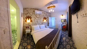 Quarto com parede de pedra, cama, mesa de cabeceira, escrivaninha, espelho e televisão.