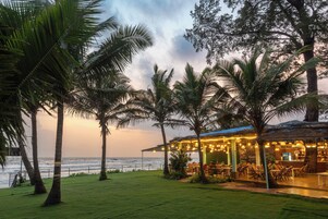Restaurante à beira-mar com área externa, palmeiras e vista para o oceano.