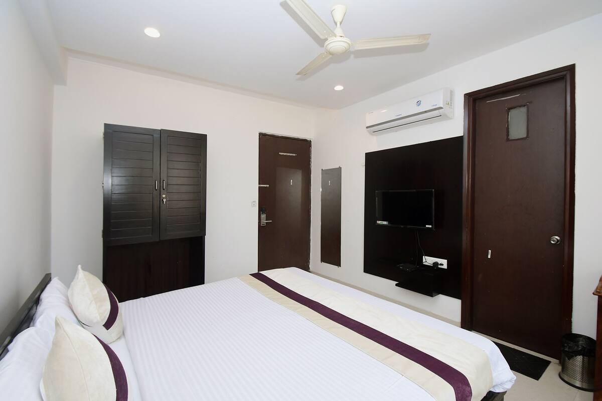 Quarto de hotel com cama, guarda-roupa, televisão e ventoinha no teto.