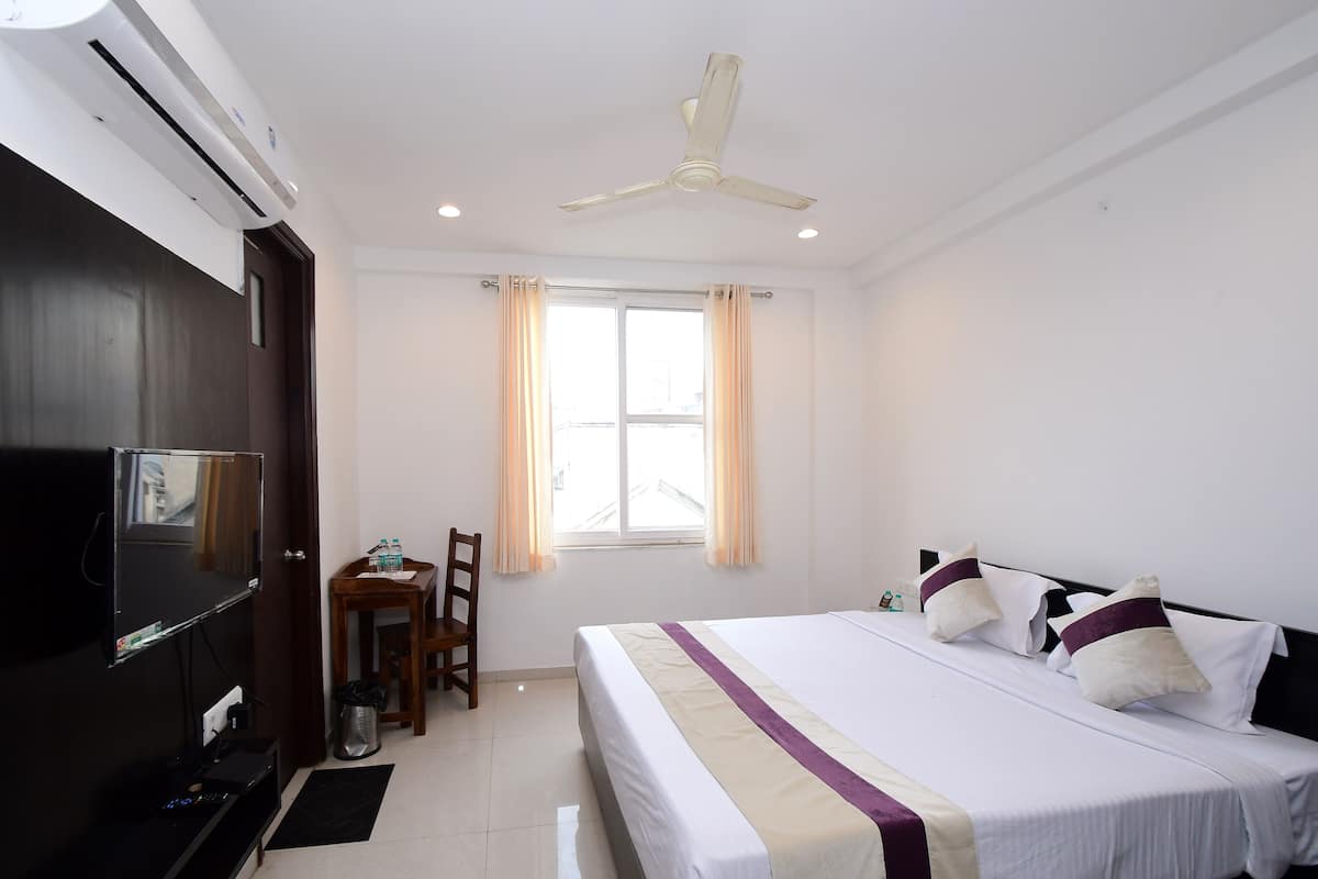 Quarto de hotel com cama, televisão, escrivaninha e janela com cortinas.