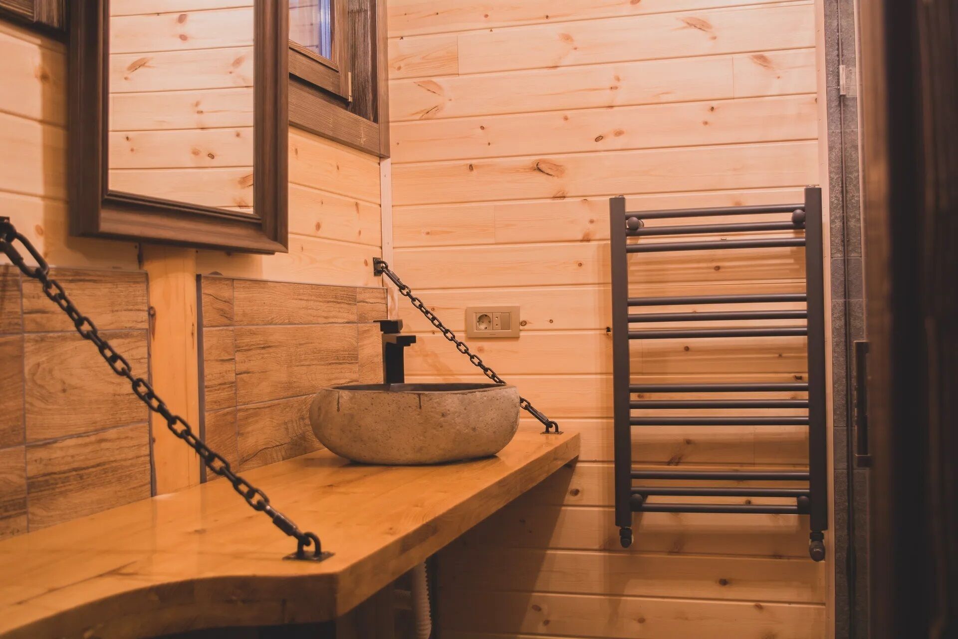 Interior de uma cabana de madeira com uma bacia de pedra, um porta-toalhas de metal e um banco de madeira.