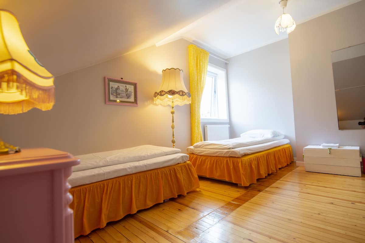 Quarto com duas camas, uma luminária, um quadro na parede e uma janela com cortinas amarelas.