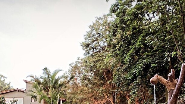 Uma área à beira da piscina com um pequeno edifício, mobiliário de exterior e vegetação exuberante.